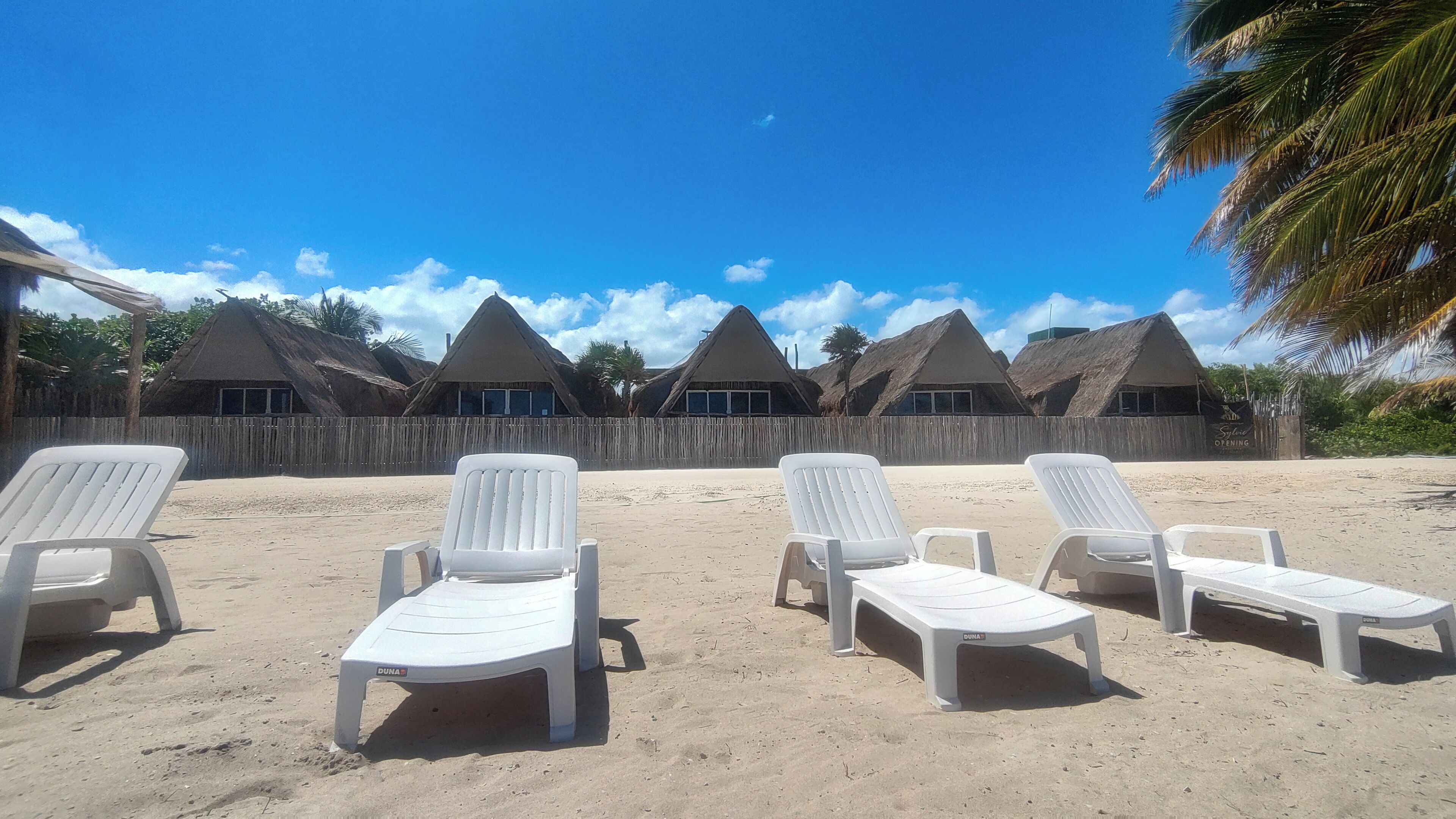 Uma praia com cadeiras de praia brancas e palafitas.