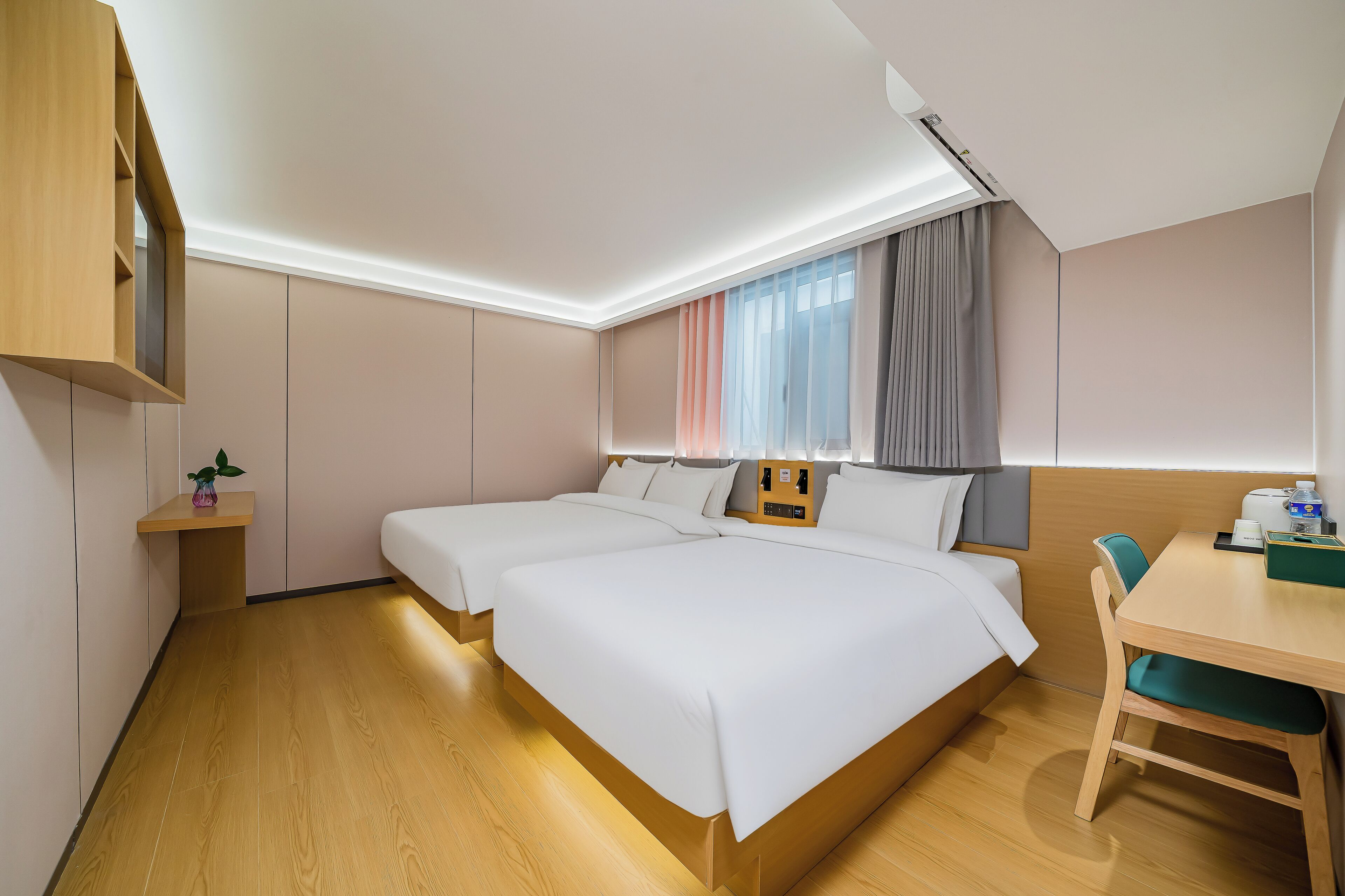 Quarto de hotel moderno com piso de madeira, duas camas de solteiro, uma escrivaninha de madeira e uma pequena planta em uma mesa de cabeceira.