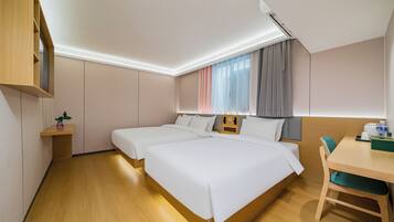 Quarto de hotel moderno com piso de madeira, duas camas de solteiro, uma escrivaninha de madeira e uma pequena planta em uma mesa de cabeceira.