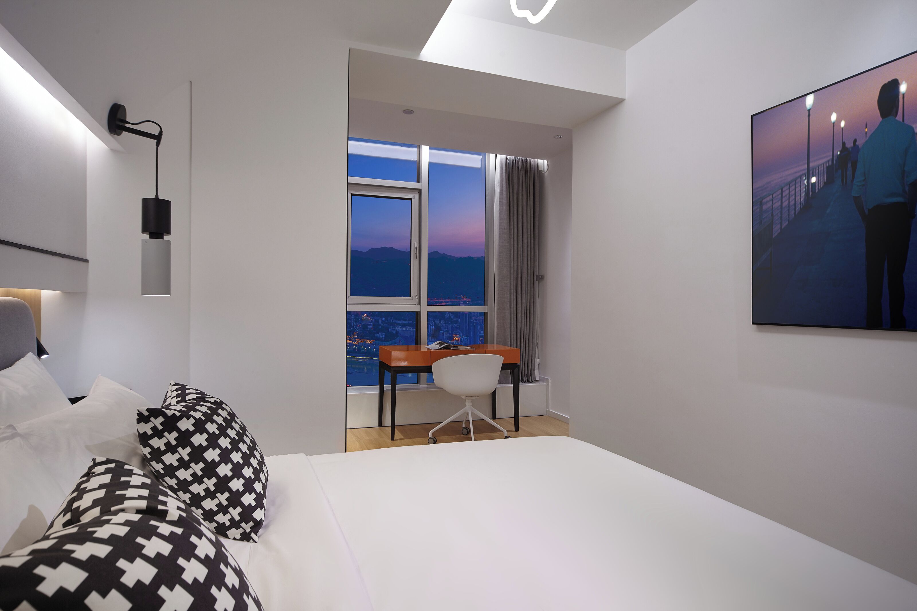 Quarto de hotel moderno com uma cama grande, uma escrivaninha e vista para a paisagem urbana através de uma grande janela.