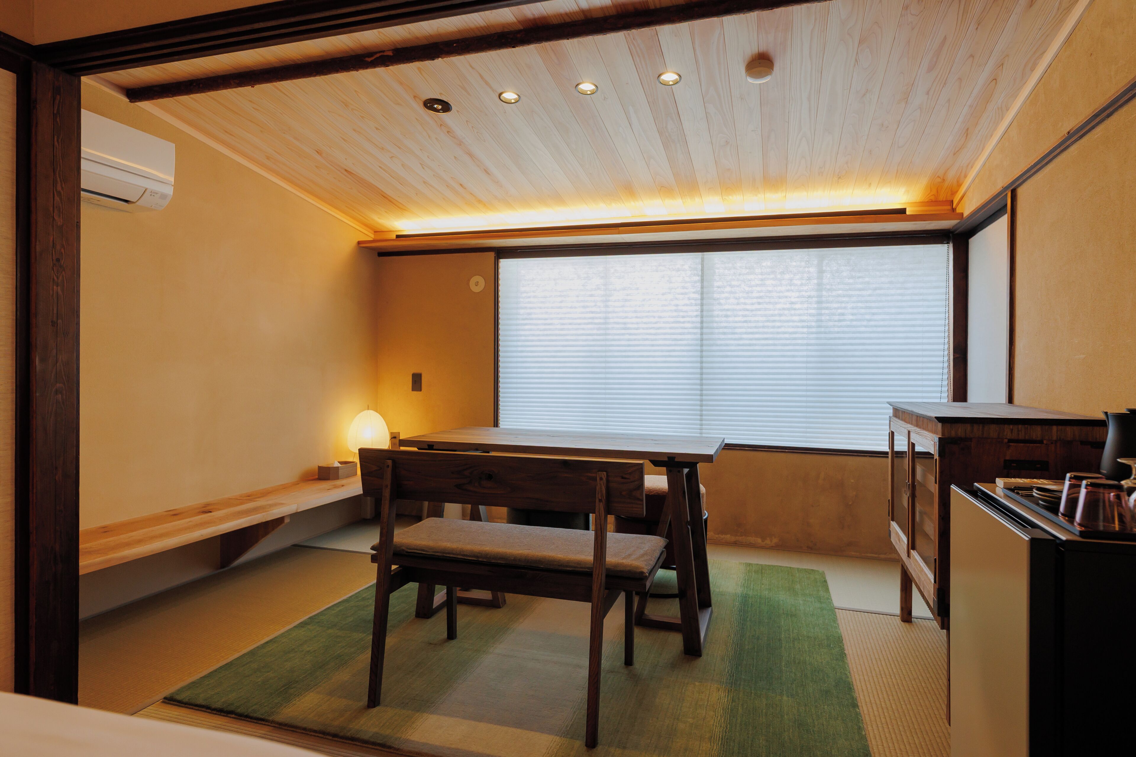 Um quarto japonês tradicional com tatames, uma mesa de madeira baixa com um banco, uma porta de papel shoji deslizante e uma área de cozinha integrada.