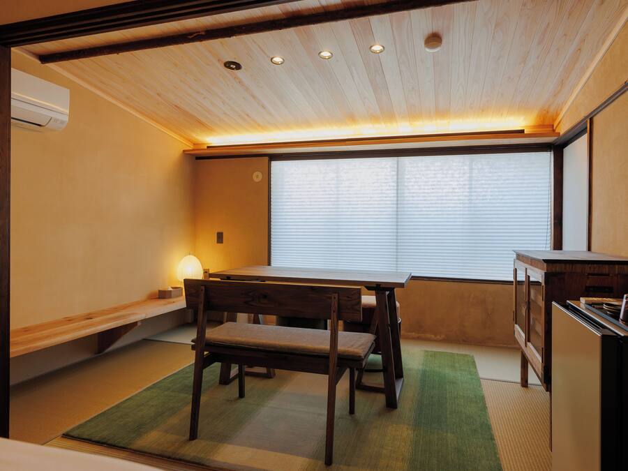 Um quarto japonês tradicional com tatames, uma mesa de madeira baixa com um banco, uma porta de papel shoji deslizante e uma área de cozinha integrada.
