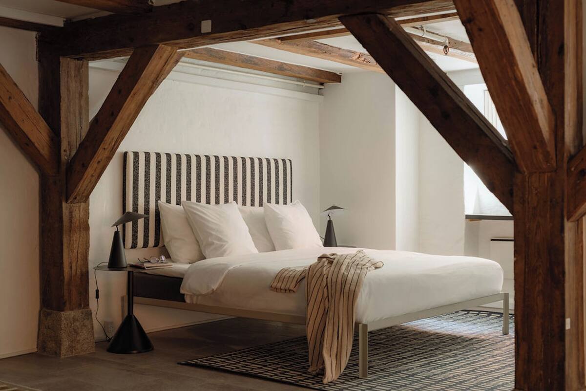 Um quarto com cama, mesas de cabeceira, abajur e tapete estampado.