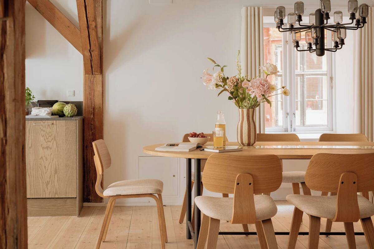Uma sala de jantar com mesa de madeira, cadeiras, um vaso com flores e um lustre.