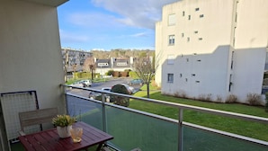 Uma varanda com mesa e cadeiras, com vista para uma rua com carros estacionados e um edifício com várias janelas.