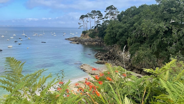 Paisagem costeira com águas cristalinas, barcos e vegetação exuberante.