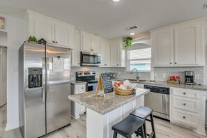 Uma cozinha moderna com armários brancos, eletrodomésticos de aço inoxidável, bancada de granito e uma ilha central com uma lousa.