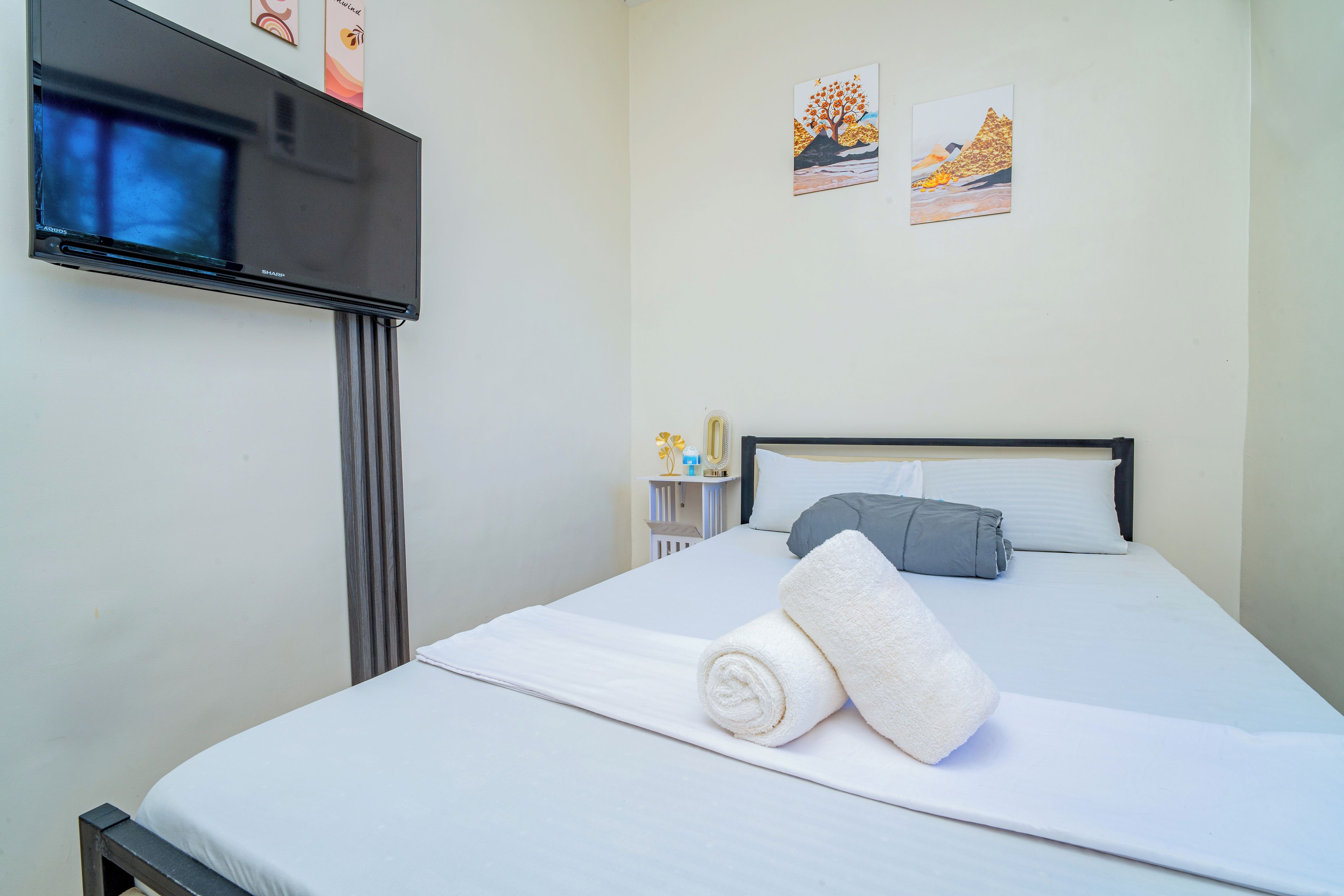 Quarto de hotel com cama, televisão de tela plana na parede e pequena mesa de cabeceira com luminária.