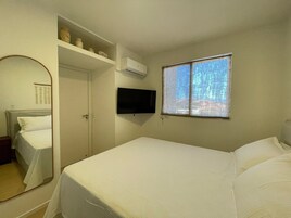 Quarto com cama, televisão na parede, janela com vista e guarda-roupa com prateleiras.