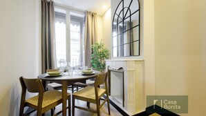Uma sala de jantar com uma mesa redonda, quatro cadeiras, um vaso de planta e uma lareira.