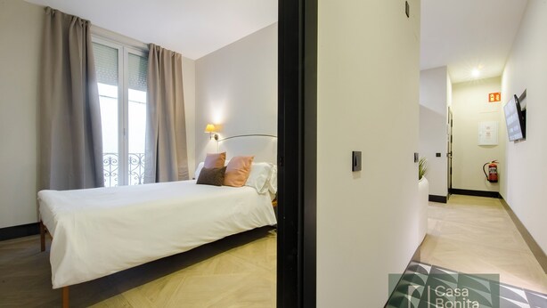 Quarto de hotel com cama, mesa de cabeceira, luminária e vista para a varanda externa.