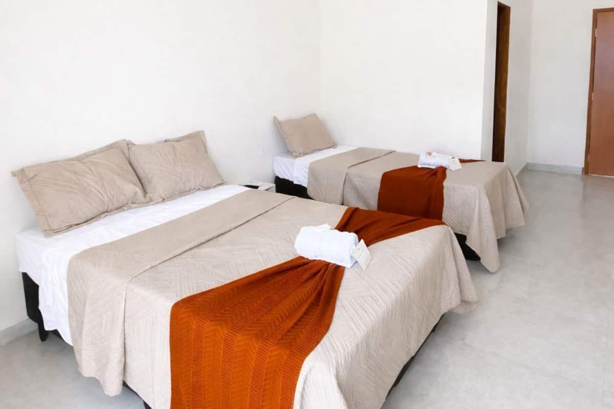 Quarto de hotel com duas camas, cada uma com colcha branca e bege, e um cobertor marrom.