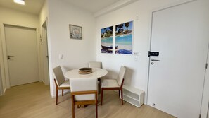 Um quarto com uma mesa redonda, quatro cadeiras, uma porta e duas imagens penduradas na parede.