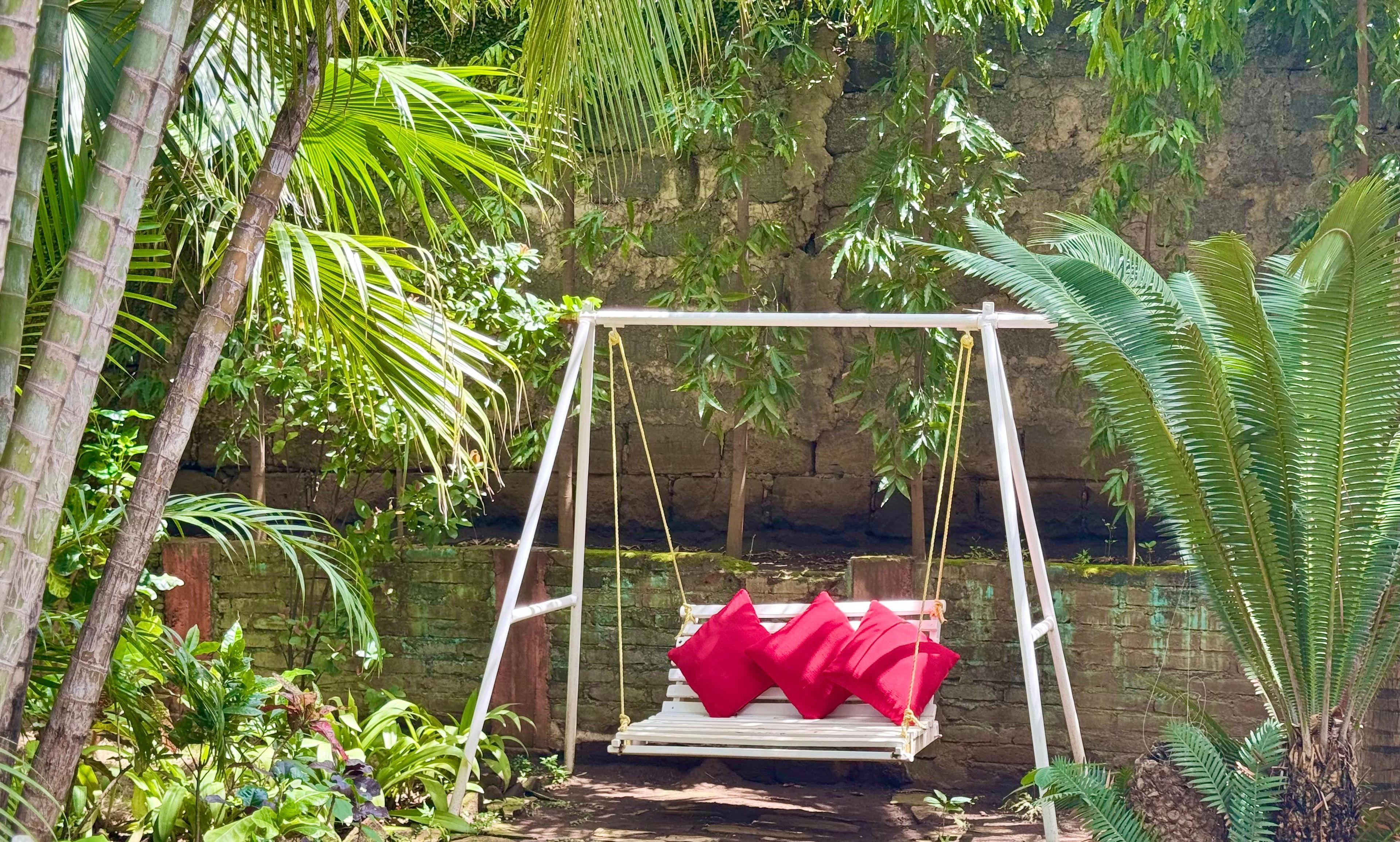 Uma cadeira balanço com almofadas vermelhas em um jardim exuberante.