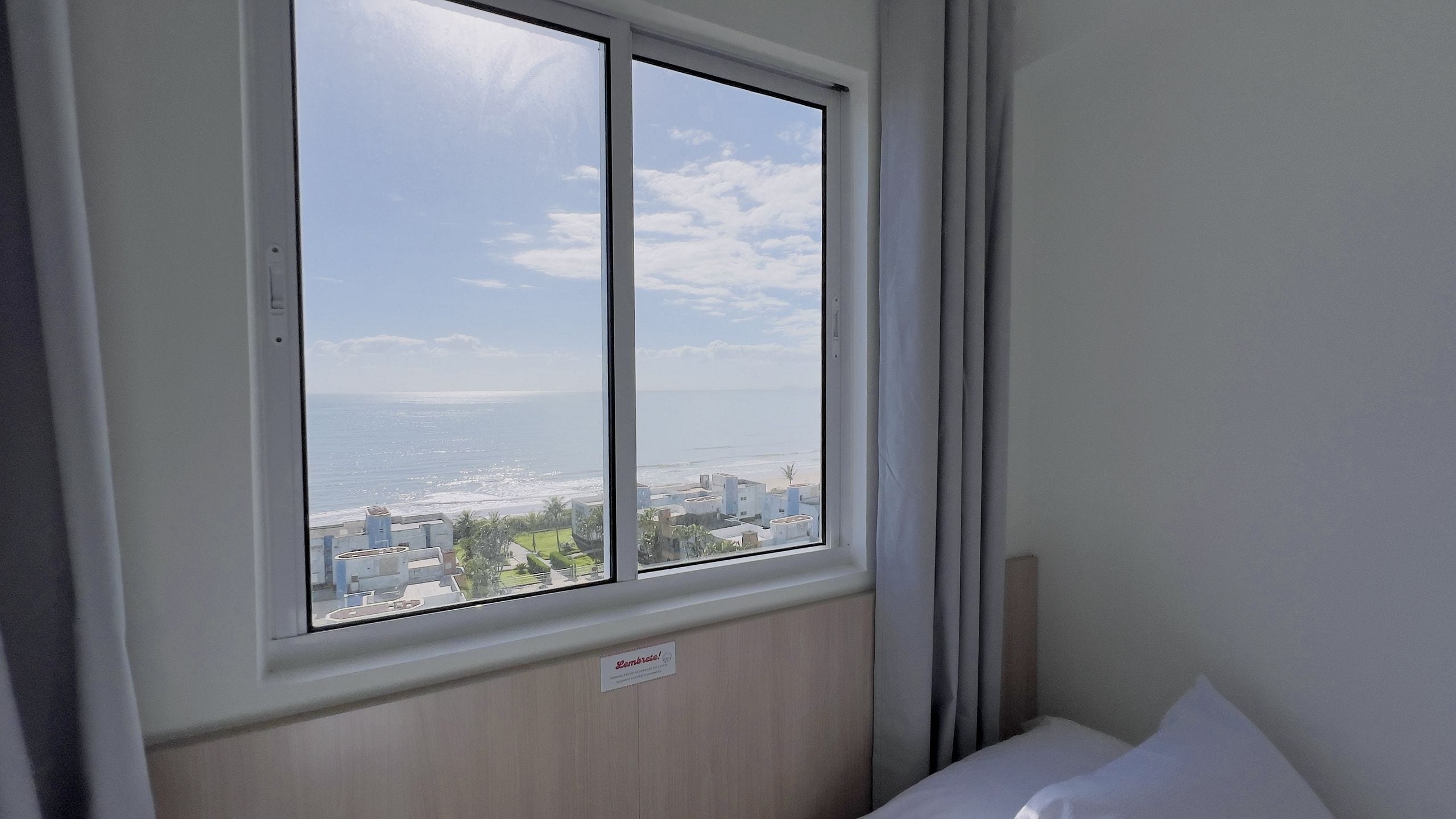 Quarto de hotel com uma janela grande que oferece vista para a cidade e o mar.