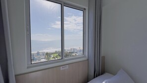 Quarto de hotel com uma janela grande que oferece vista para a cidade e o mar.