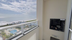 Varanda com vista para a praia e o oceano, piscina e churrasqueira ao ar livre.