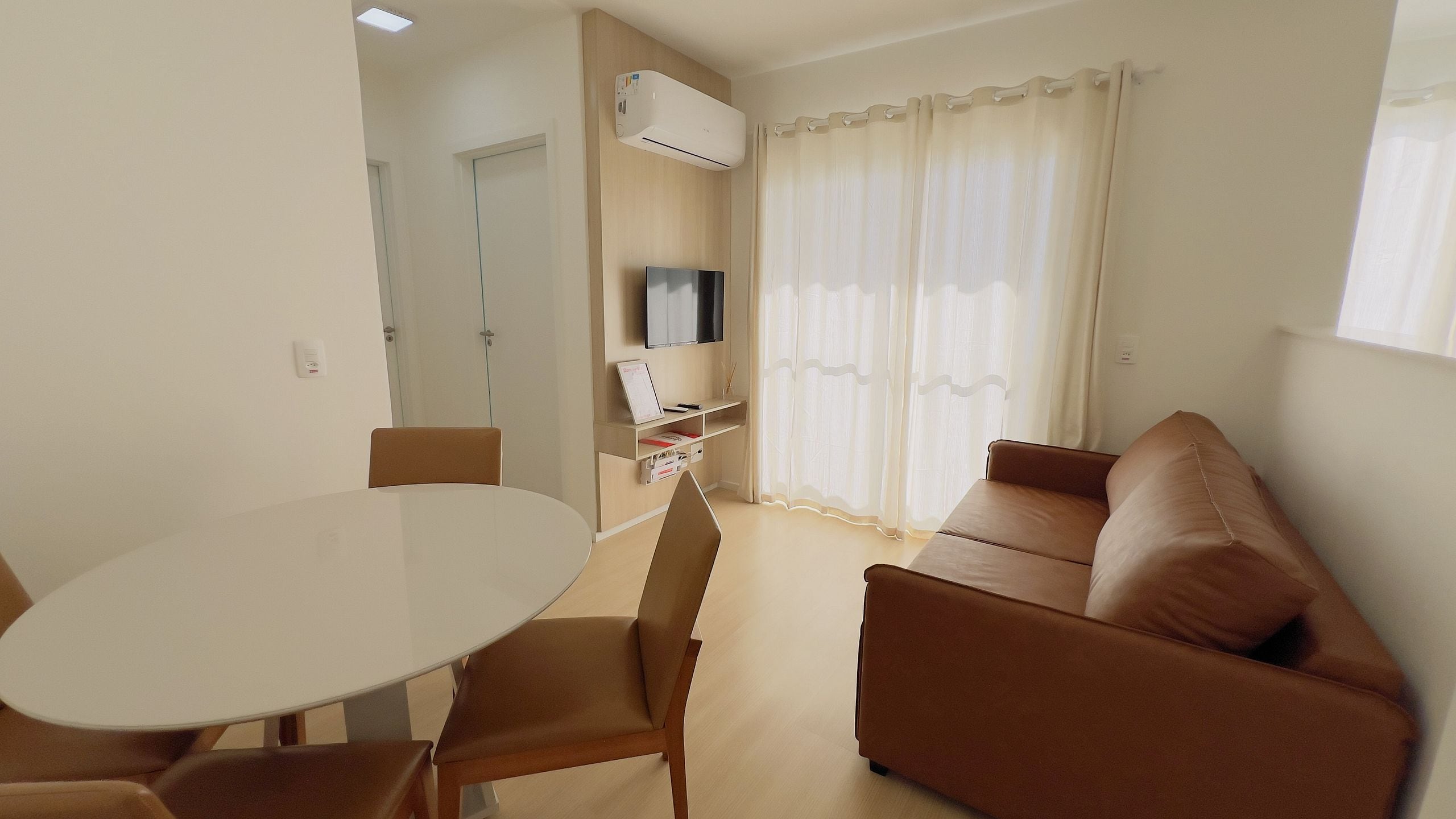 Uma sala de estar moderna com uma mesa de jantar redonda, sofá de couro marrom e televisão na parede.