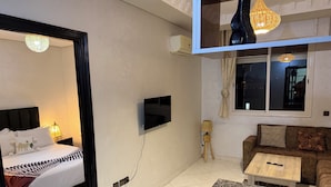 Quarto com cama, televisão, sofá, mesa de centro e mesa de jantar.