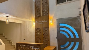 Uma área de recepção com um balcão de madeira identificado com a placa “Reception”, uma parede com um painel decorativo e uma porta com um design circular azul.