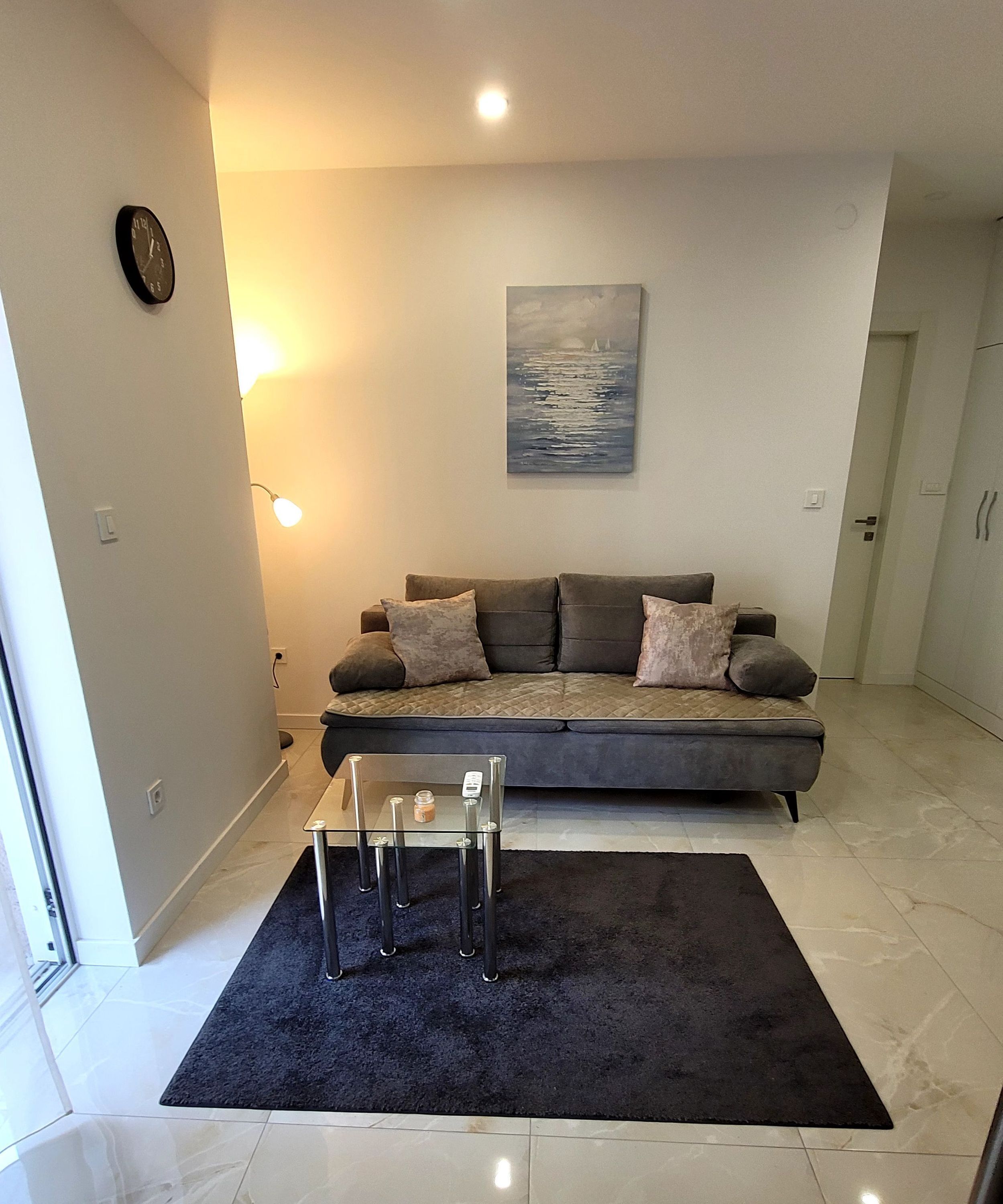 Uma sala de estar moderna com um sofá cinzento, uma mesa de centro de vidro e um quadro na parede.