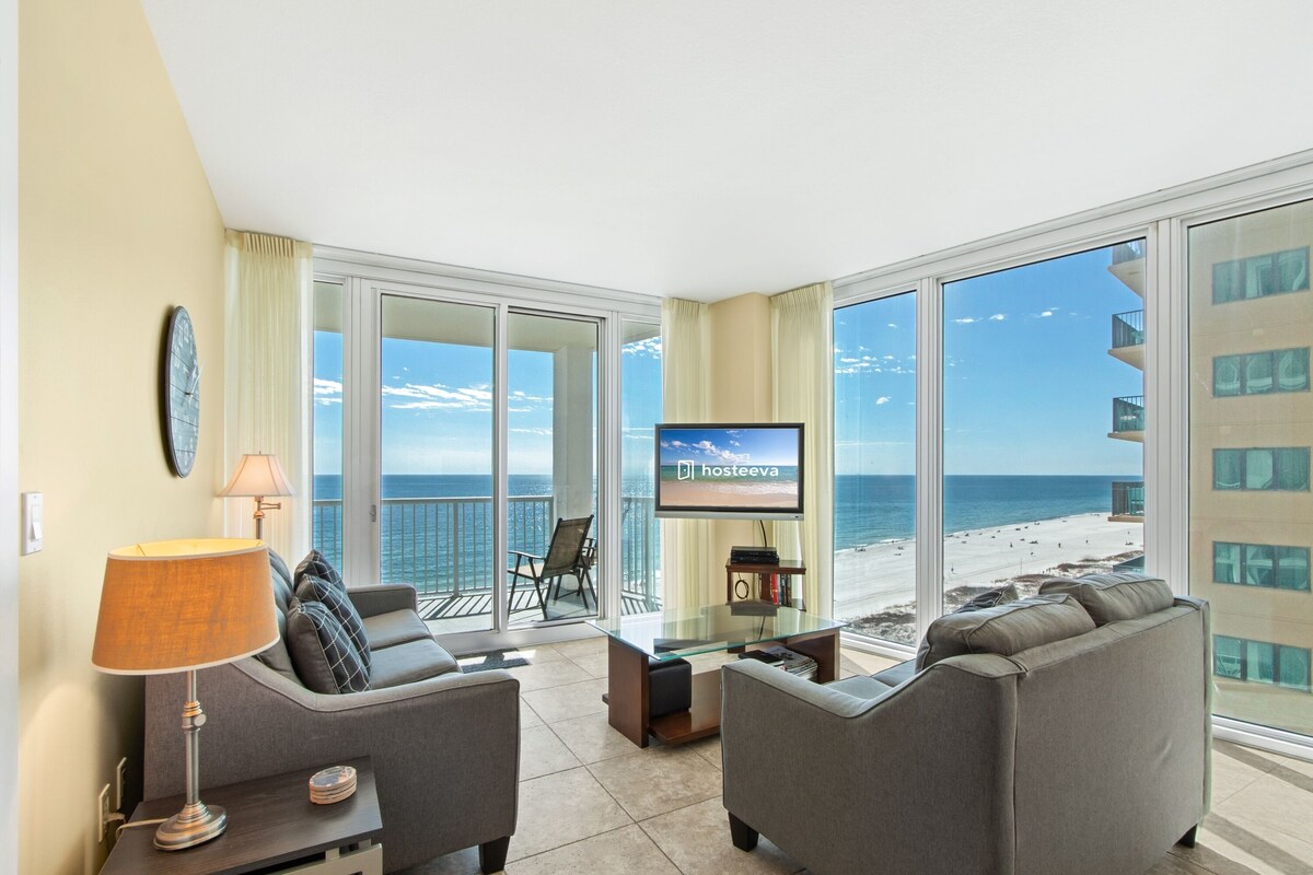 Sala de estar moderna com uma televisão grande, assentos confortáveis e uma varanda com vista para a praia.