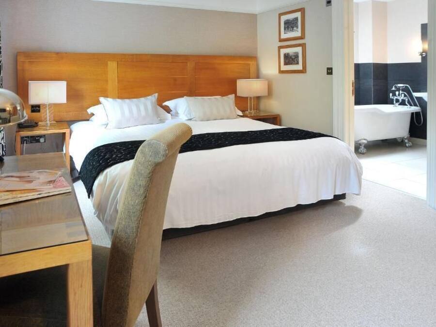 Quarto de hotel com uma cama grande, duas mesas de cabeceira com luminárias, uma escrivaninha com cadeira e um banheiro visível por uma porta aberta.