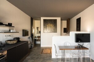 Cozinha moderna com painel de backsplash de pedra, ilha de madeira e área de jantar com cadeiras transparentes e uma TV.