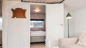 Quarto com cama, mesa de cabeceira com luminária, cabeceira de madeira e janela com persianas.