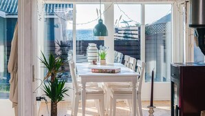 Uma sala de jantar com uma mesa, cadeiras, uma luminária pendente e vista para o mar.