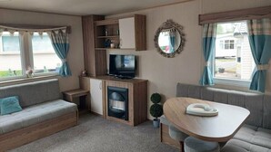 Interior compacto de uma RV com um sofá, uma mesa pequena, uma televisão e uma lareira.