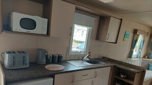 Uma cozinha compacta com micro-ondas, torradeira, chaleira e pia.
