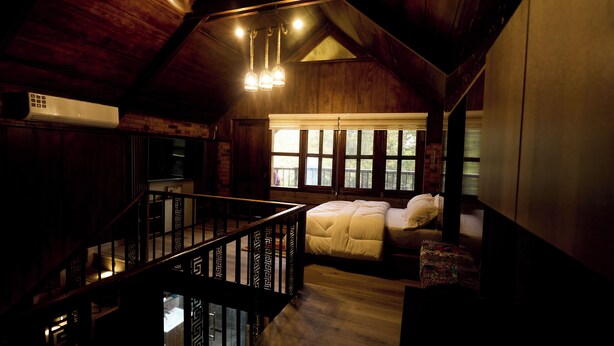 Quarto com cama grande, escada de madeira e vista para o exterior pelas janelas.