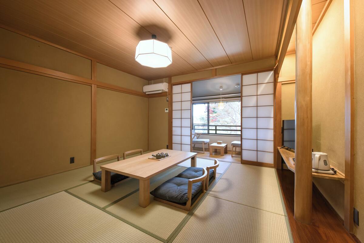 Um quarto japonês tradicional com tatame, uma mesa de madeira baixa, almofadas e portas deslizantes shoji.