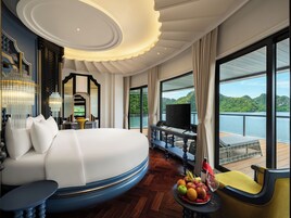Um quarto luxuoso com uma cama grande, televisão e área de refeições com vista para a água.
