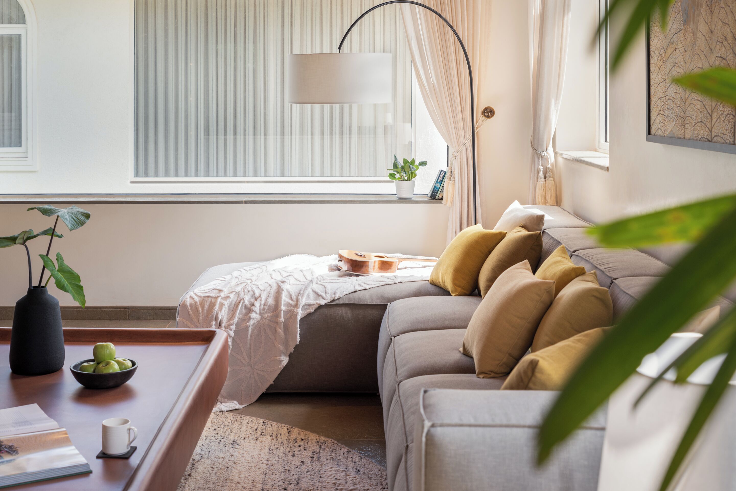 Uma sala de estar moderna com sofá, mesa de centro, abajur, planta e janela com cortinas.
