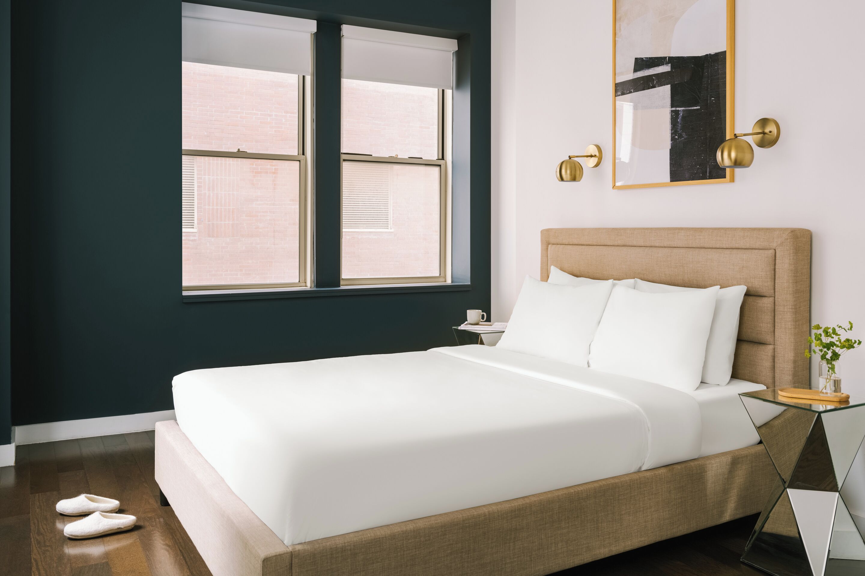 Quarto com cama, mesa de cabeceira, janela e espelho fixado na parede.