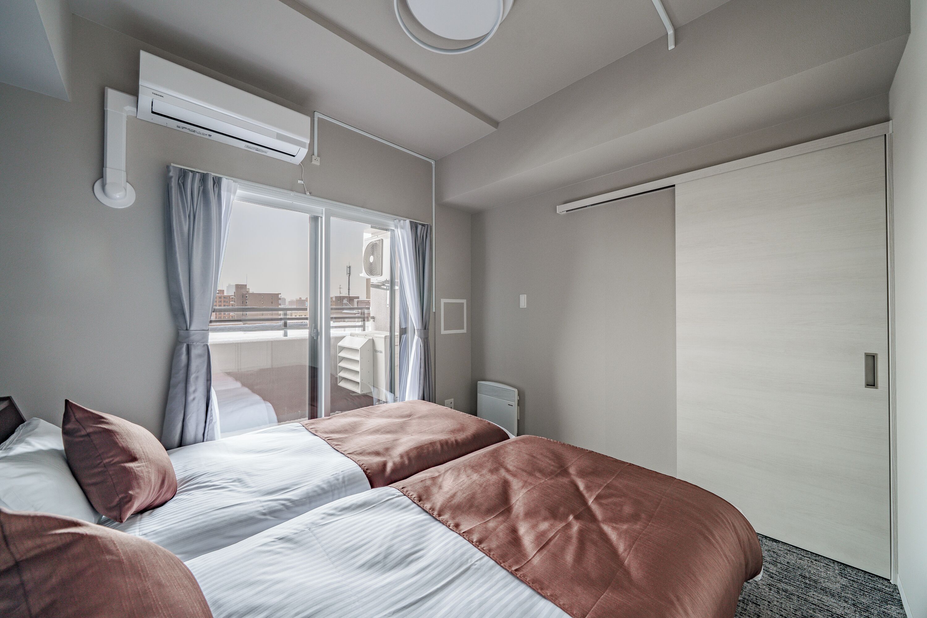 Quarto de hotel com cama, janela com cortinas, ar condicionado e porta.