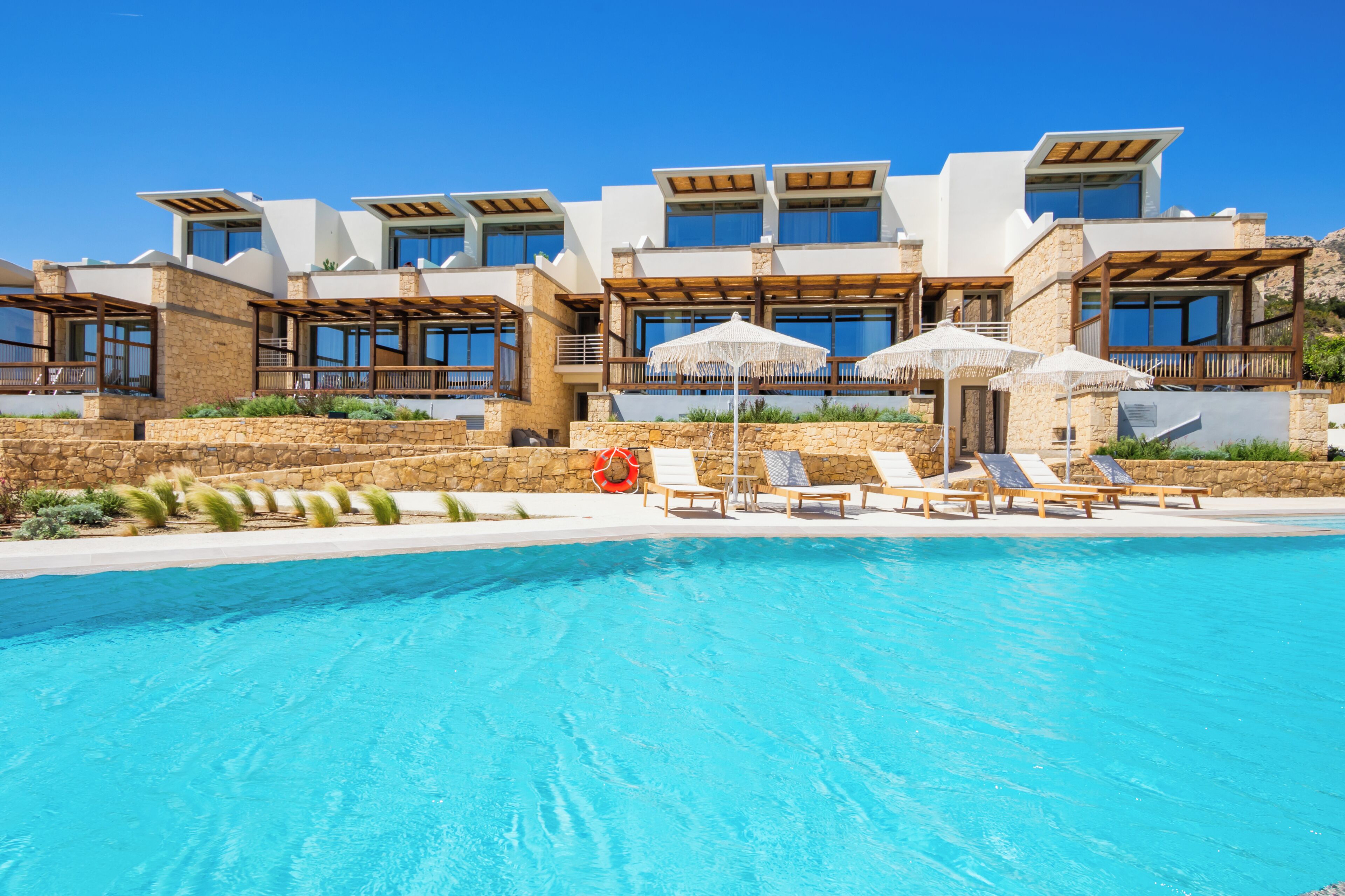 Um hotel moderno com piscina, área de estar externa e céu azul límpido.