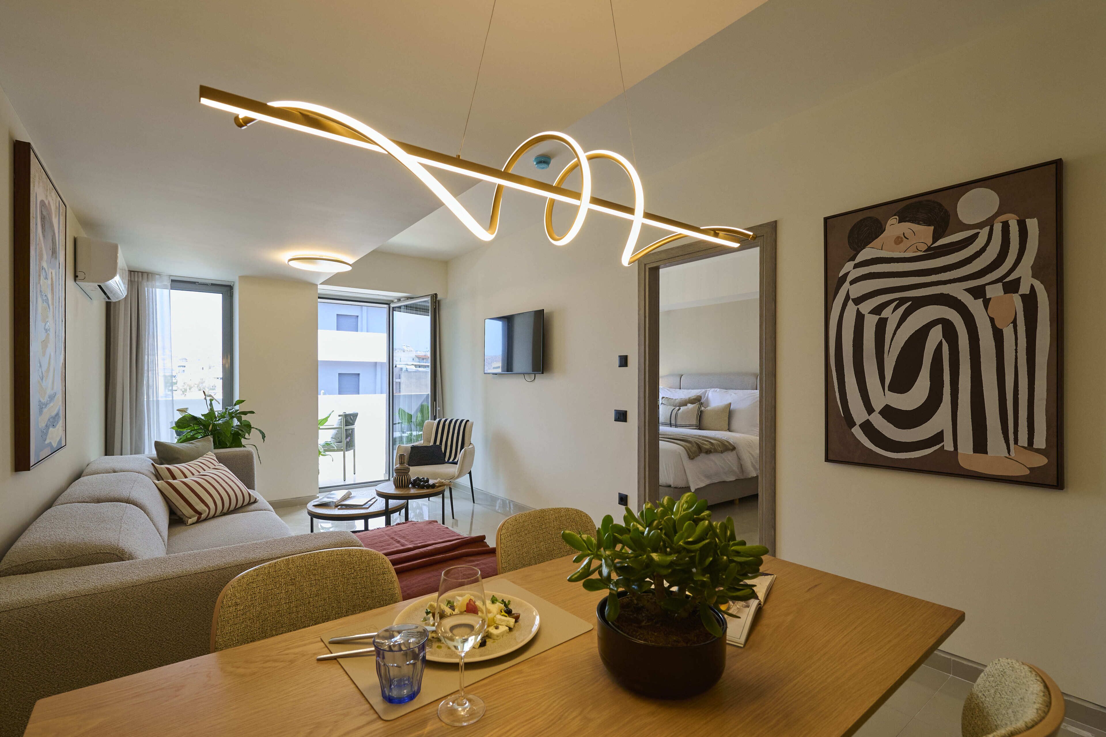 Quarto de hotel moderno com área de refeições, sofá, planta em vaso e um quadro na parede.
