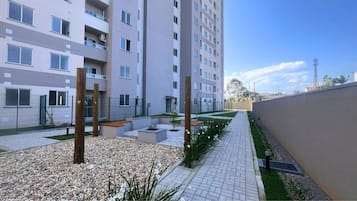 Um edifício residencial com vários andares, varandas, um pátio pavimentado e um jardim ajardinado.