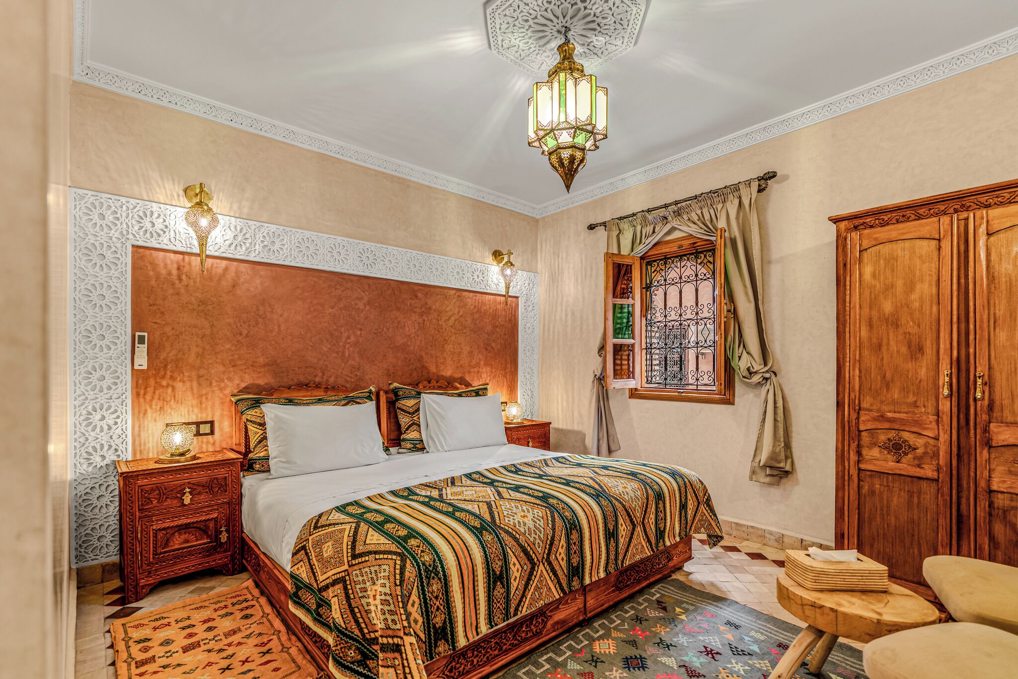 Quarto tradicional com cama, guarda-roupa de madeira, janela com grades decorativas de ferro e tapete estampado.