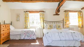 Quarto com duas camas, cómoda de madeira, cortinas florais e vigas de madeira aparente.
