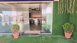 Um lobby de hotel moderno com entrada de vidro, plantas em ambiente interno e vista para a rua.