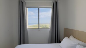 Quarto de hotel com cama, janela com cortinas e vista para a paisagem.