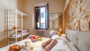 Quarto de hotel com cama, armário, janela com cortinas, parede de pedra e bandeja com itens de café da manhã.