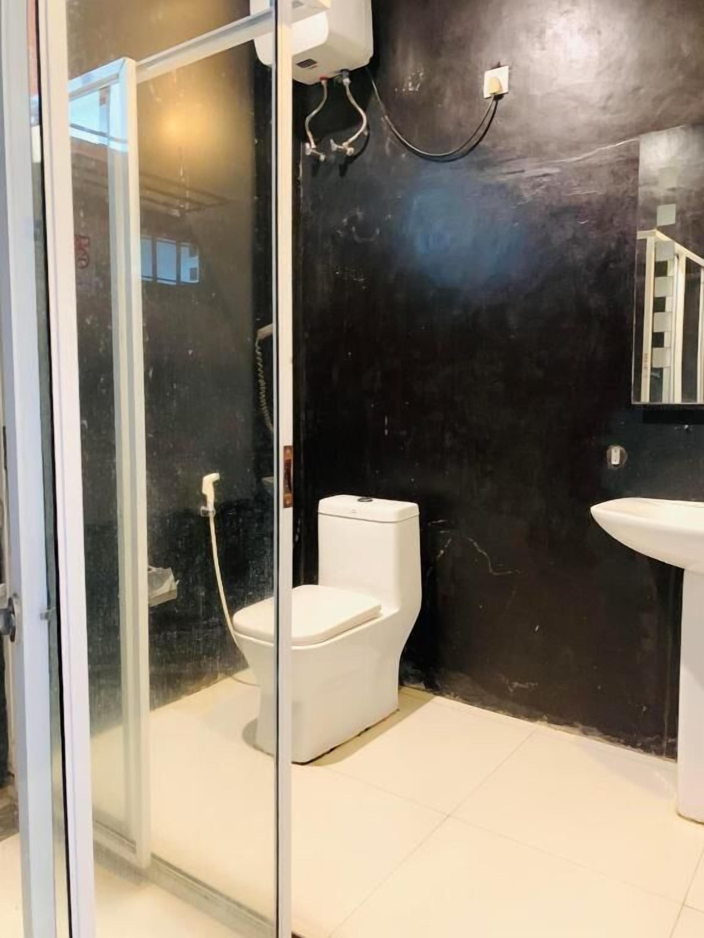Casa de banho com cabine de duche em vidro, sanita branca e lavatório branco, tudo contra uma parede escura.