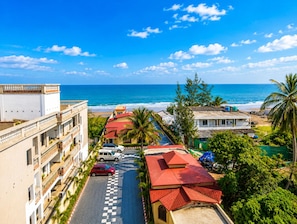 Uma rua costeira com edifícios, uma praia e um céu claro.