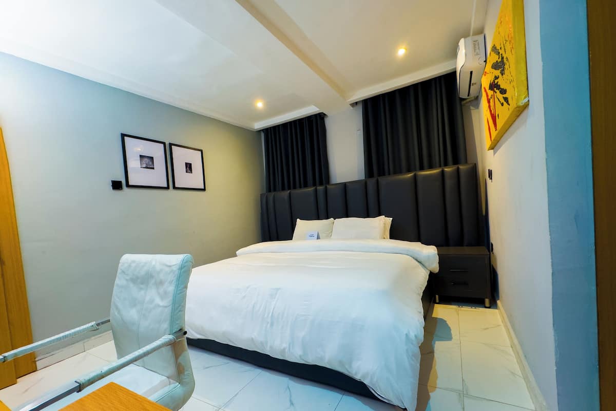 Quarto de hotel com uma cama, uma cadeira, uma escrivaninha e um quadro na parede.