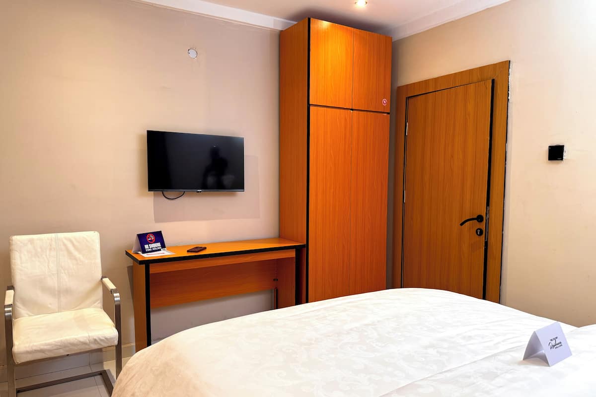 Quarto de hotel com cama, secretária com cadeira, televisão fixada na parede e guarda-roupa de madeira.